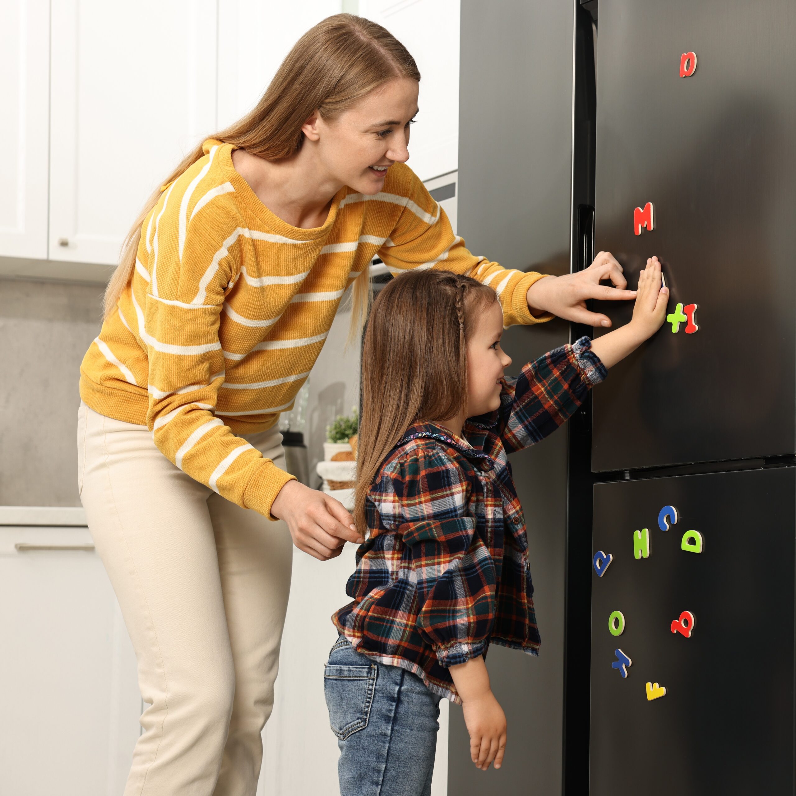 Mom and daughter putting magnetic letters on fridge at home. Learning ...